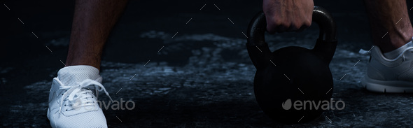 cropped view of muscular bodybuilder excising with kettlebell on black ...