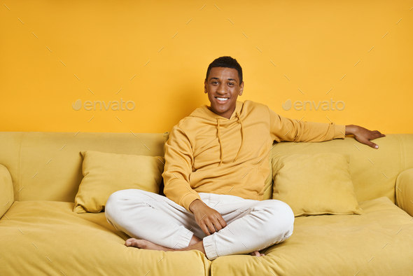 Happy mixed race man relaxing on the couch with yellow background Stock ...