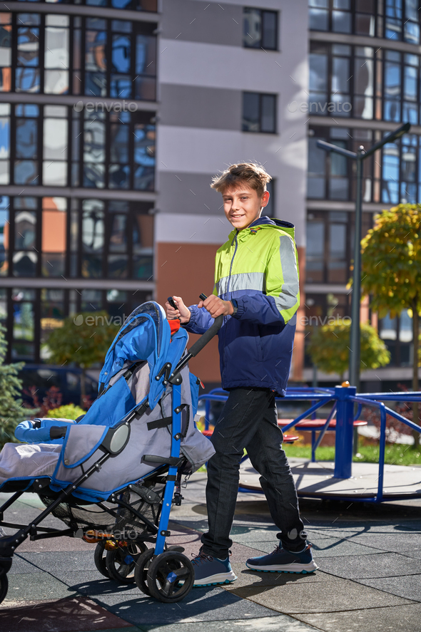 Teen boy walking with baby brother in stroller outdoor. Stock Photo by ...