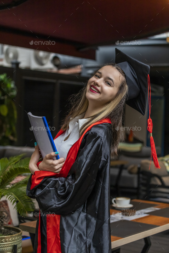 Portrait of beautiful student holding notebook and wearing graduation ...