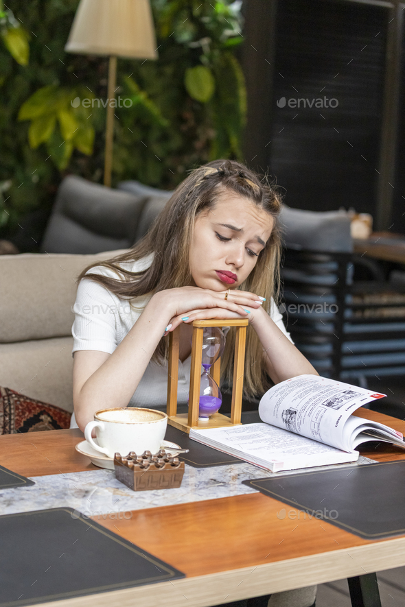 Vertical photo of young beautiful lady holding hourglass and reading ...