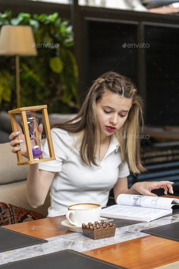 Vertical photo of young lady holding hourglass and reading her book ...