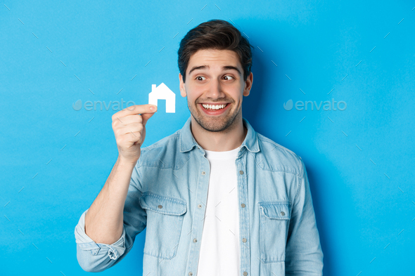 Real estate concept. Excited guy looking at small house model and ...