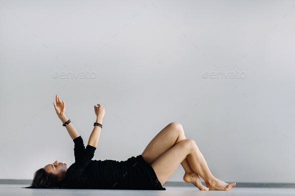 A girl in a black dress lying down moves in a dance on the floor ...