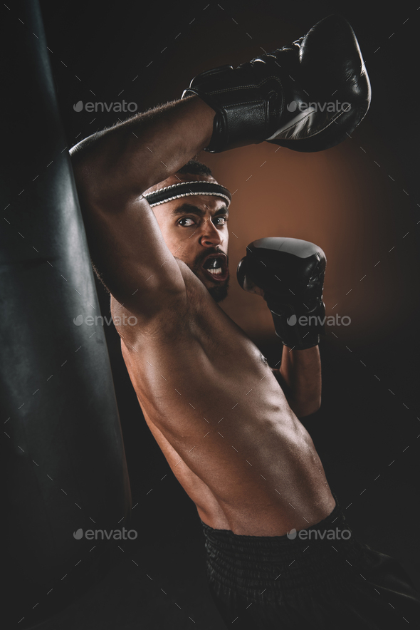 Aggressive young Muay Thai fighter in boxing gloves training thai ...