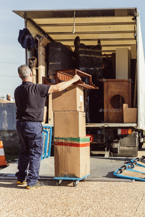 older worker brings a pile of cardboard boxes to a truck in a moving ...
