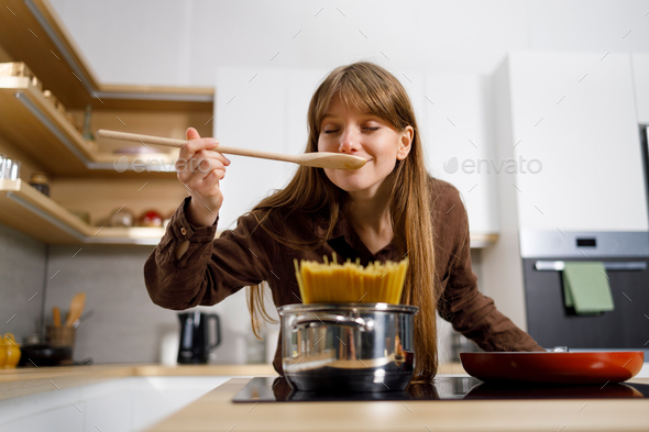 Cheerful girl is tasting food while cooking in kitchen at home Stock ...