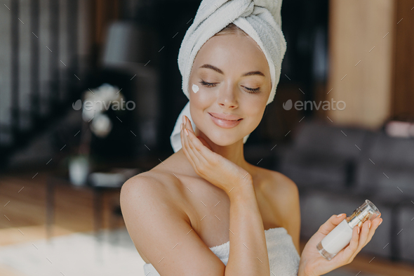 Close up shot of young feminine lady applies face lotion, wears wrapped ...