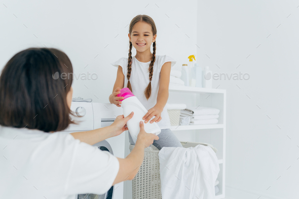 Happy child helper and mother have fun in laundry room, do washing ...