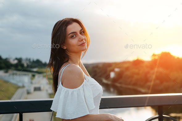 Portrait of pretty young brunette woman standing on bridge against ...