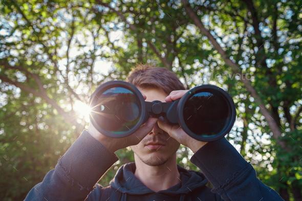 Explorer hiker young man in plaid shirt looking through binoculars ...