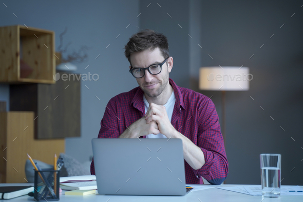 Pensive young German man home office employee sits at desk at workplace ...