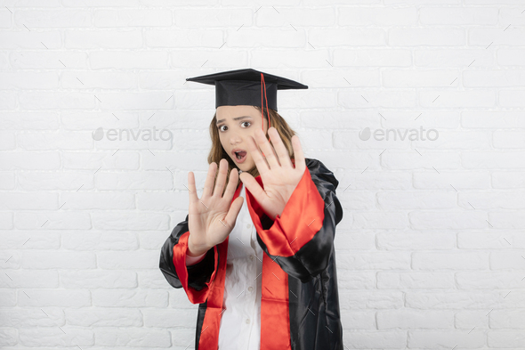 Scared young girl wearing graduation gown and gesturing stop. Stock ...