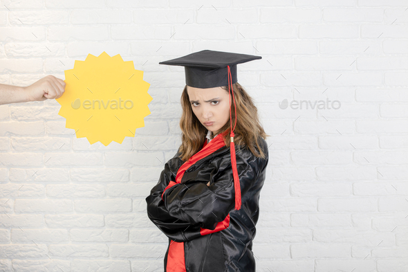 Upset young student wearing graduation gown and stand on beside of sun ...