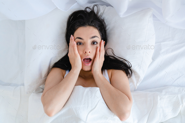 Scared young beautiful woman lying in the bed because of the ...