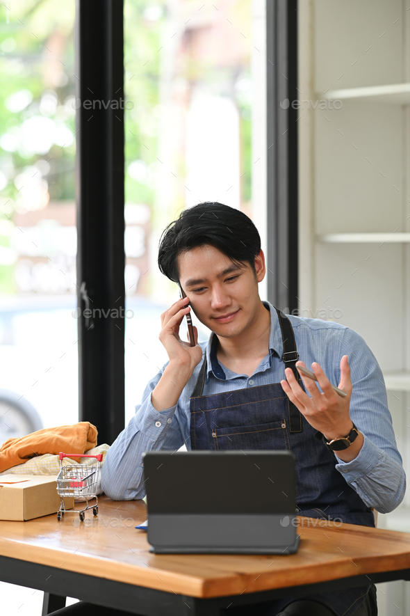 Young small business owner using computer and talking on mobile phone ...