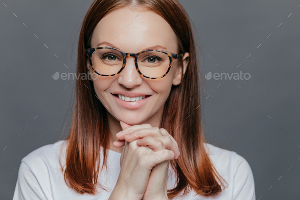 happy young European woman has pleasant smile, keeps hands together ...