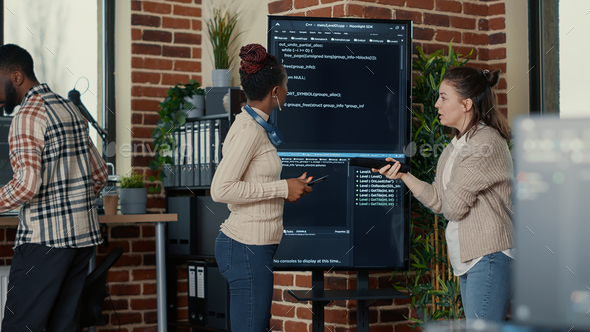 Programmer holding digital tablet analyzing code on wall screen tv ...
