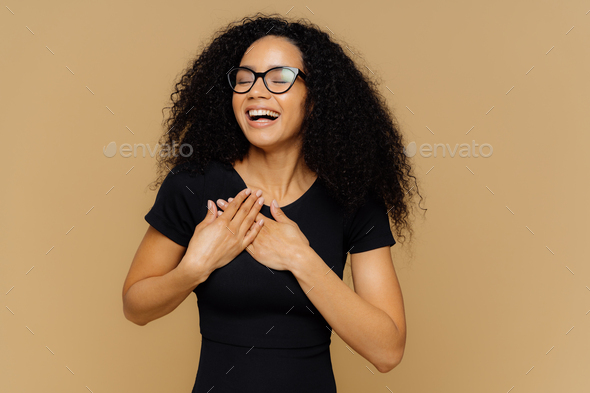 Thankful positive woman smiles happily, makes gratitude gesture, keeps ...