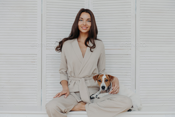 Horizontal shot of pretty relaxed woman dressed in beige costume, plays ...