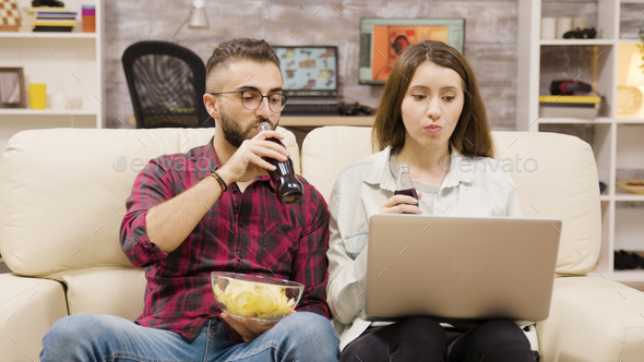Couple drinking soda and eating chips while browsing on laptop Stock ...