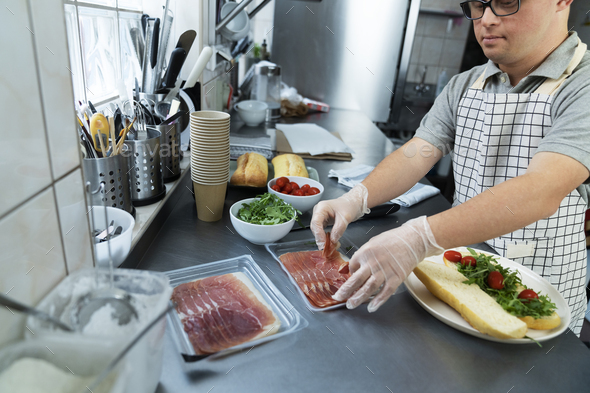 Caucasian man with down syndrome preparing a sandwich in commercial ...