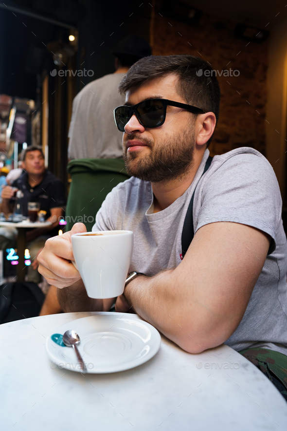 Handsome man drinking coffee in outdoor cafe Stock Photo by FabrikaPhoto