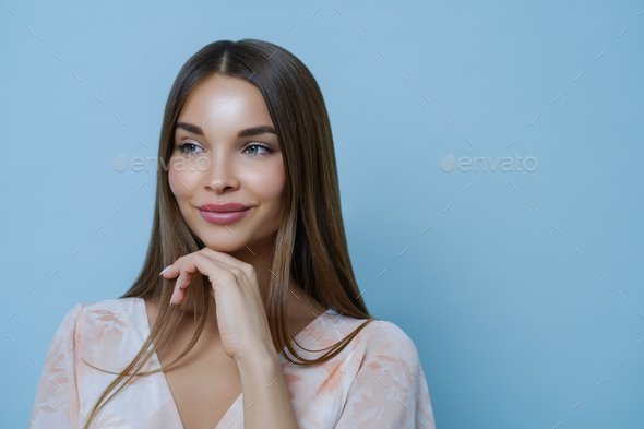 Portrait of good looking woman touches chin and has thoughtful ...