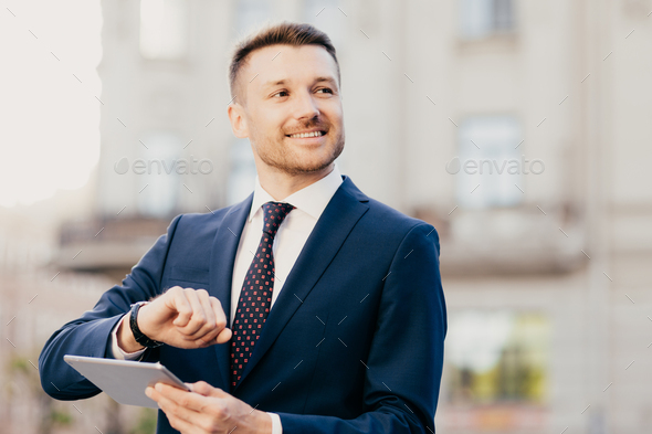 Attractive male business owner in elegant black suit, looks at ...