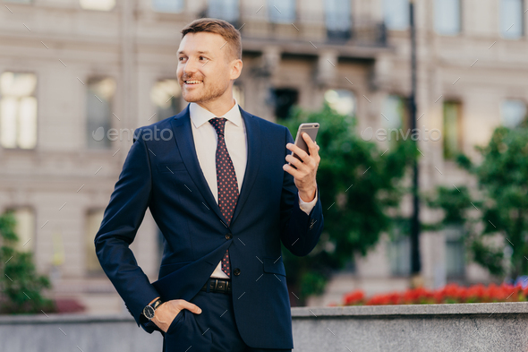 Happy attractive male financier in elegant wear, uses modern smartphone ...