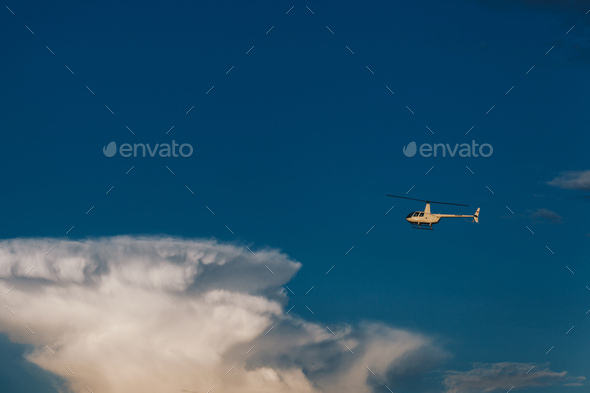 Horizontal shot of white helicopter flies high in blue sky with clouds ...