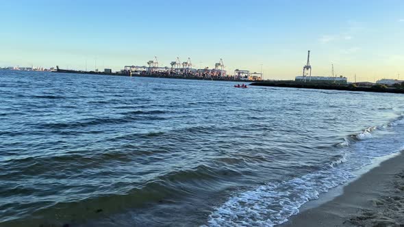 A small boat moves along the ocean with Port Melbourne docks in the ...