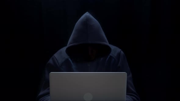 The hacker uses a laptop. A hooded mysterious man with an invisible ...