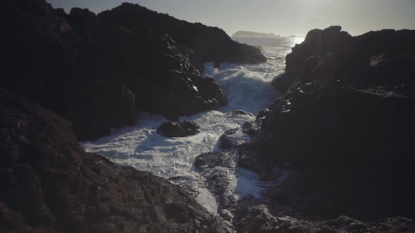 Medium tilt up shot of splashing ocean wave on rocks at sunny day in ...