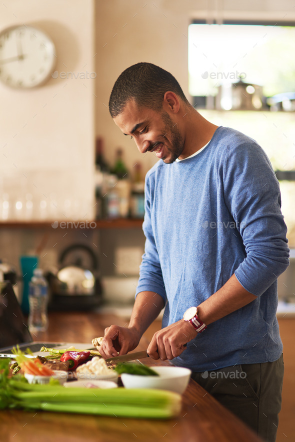 Making a healthy meal from scratch. Shot of a happy young man preparing ...