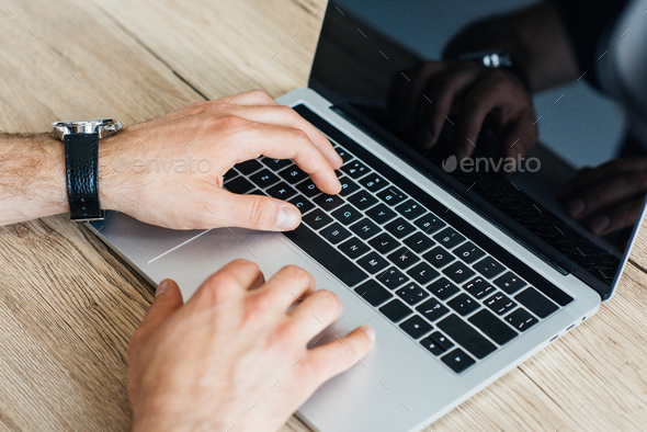 close-up partial view of person typing on laptop with blank screen ...