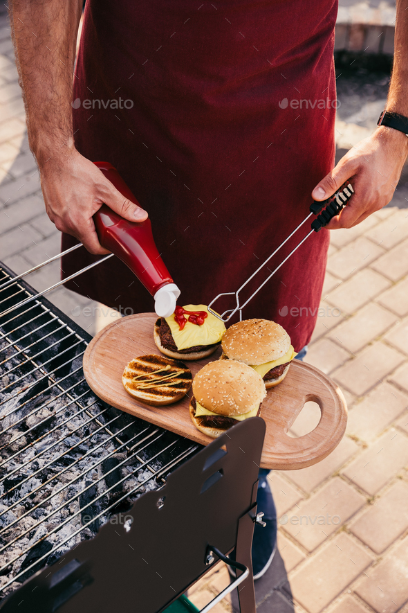 Chef adding ketchup to burgers grilled for outdoors barbecue Stock ...