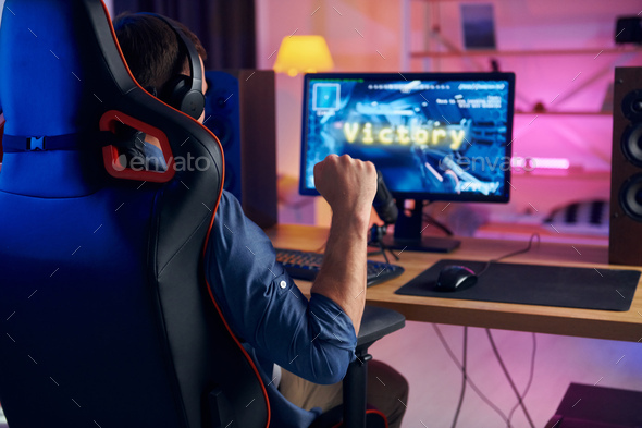 Sitting on the chair. Online streamer playing FPS shooter game at home ...