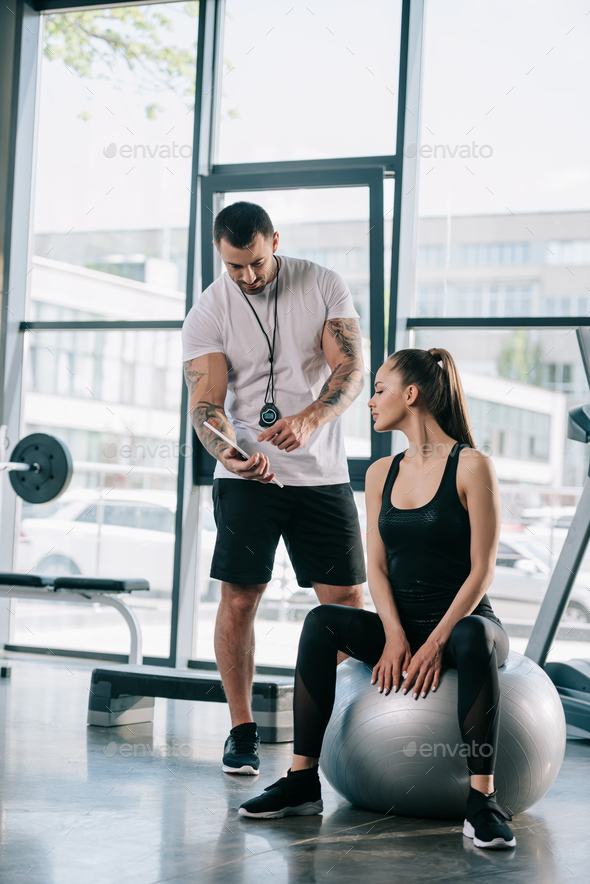 trainer pointing on digital tablet screen to young sportswoman sitting ...