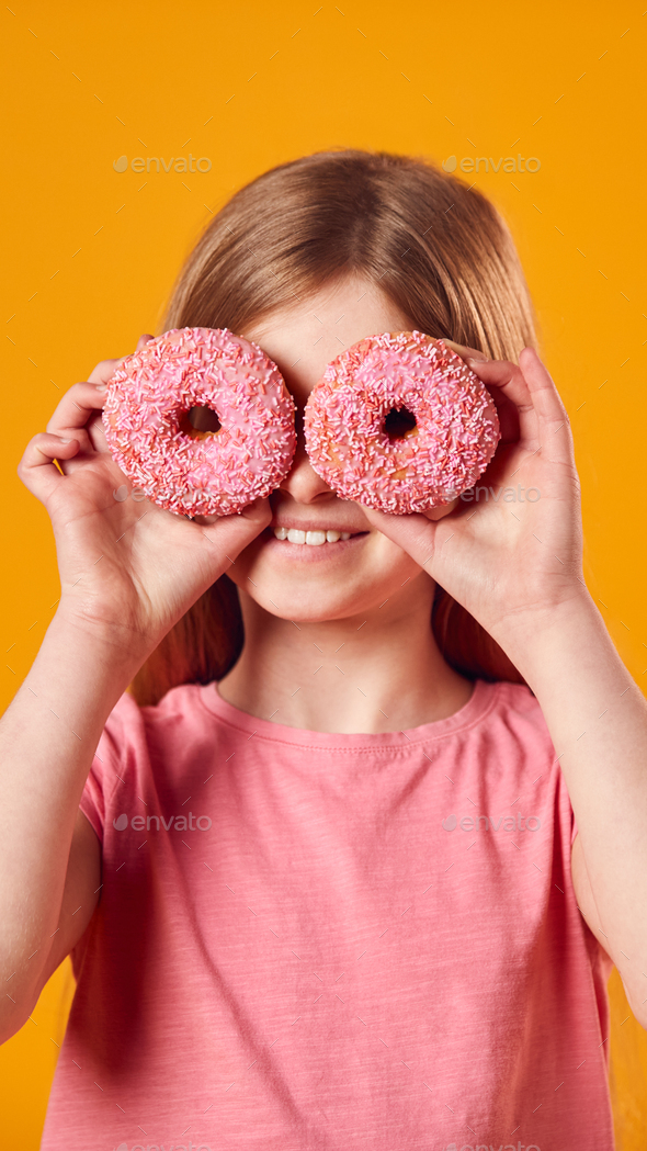 Studio Portrait Of Girl Holding Two Donuts In Front Of Eyes Against ...