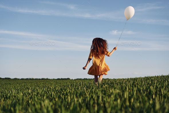 Holding balloon in hand. Happy girl have a walk outdoors on the field ...