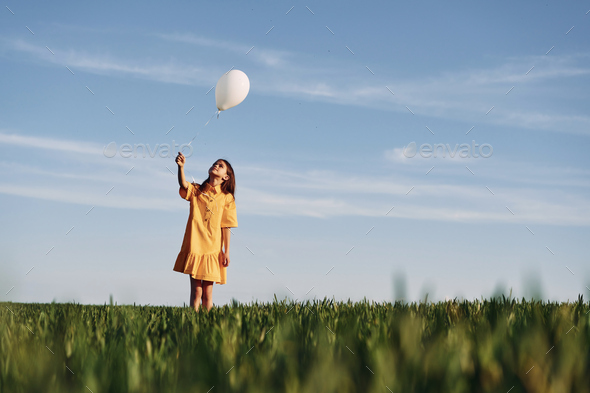 Holding balloon in hand. Happy girl have a walk outdoors on the field ...
