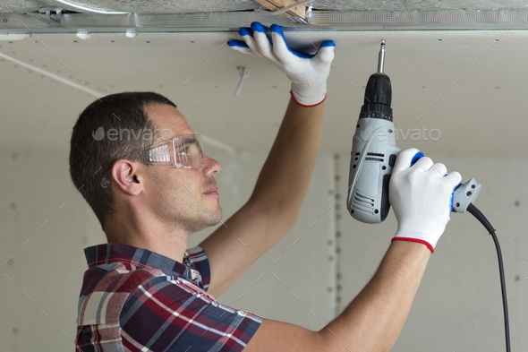 Young man fixing drywall suspended ceiling to metal frame using ...