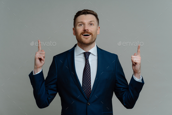 Shocked businessman in suit pointing up with fingers and looking with ...