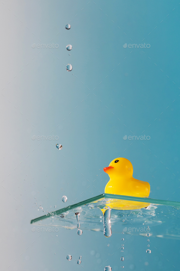 Yellow rubber duck on glass shelf and dripping water on light blue ...