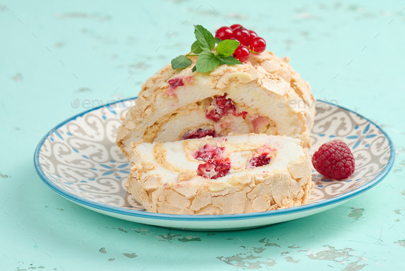 Baked meringue roll with red berries on a round plate, white background ...