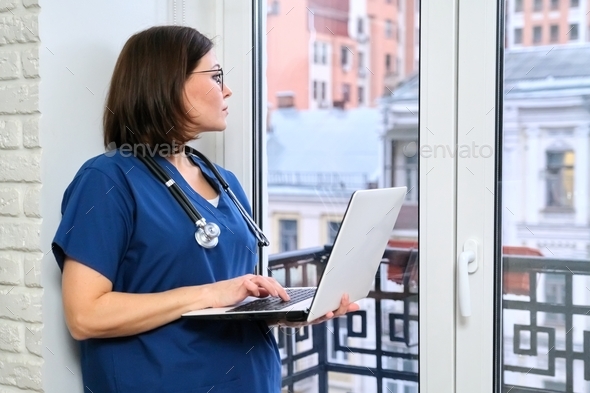 Female nurse using laptop computer, doctor near window in clinic office ...