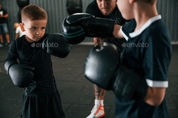 Having fun by practicing. Young tattooed coach teaching the kids boxing ...