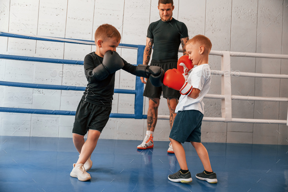 Fighting on the ring. Young tattooed coach teaching the kids boxing ...