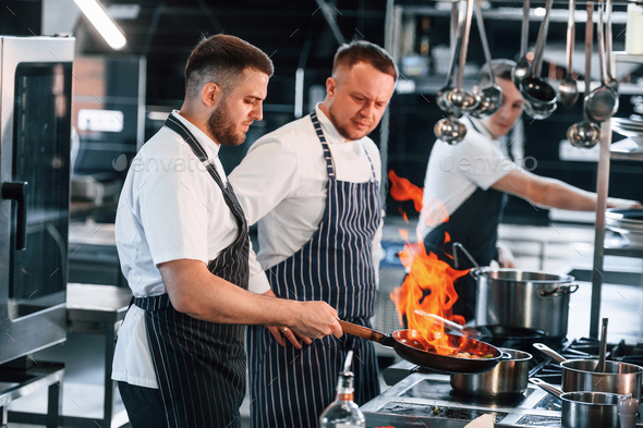 Flaming the meal on frying pan. Kitchen workers is together preparing ...
